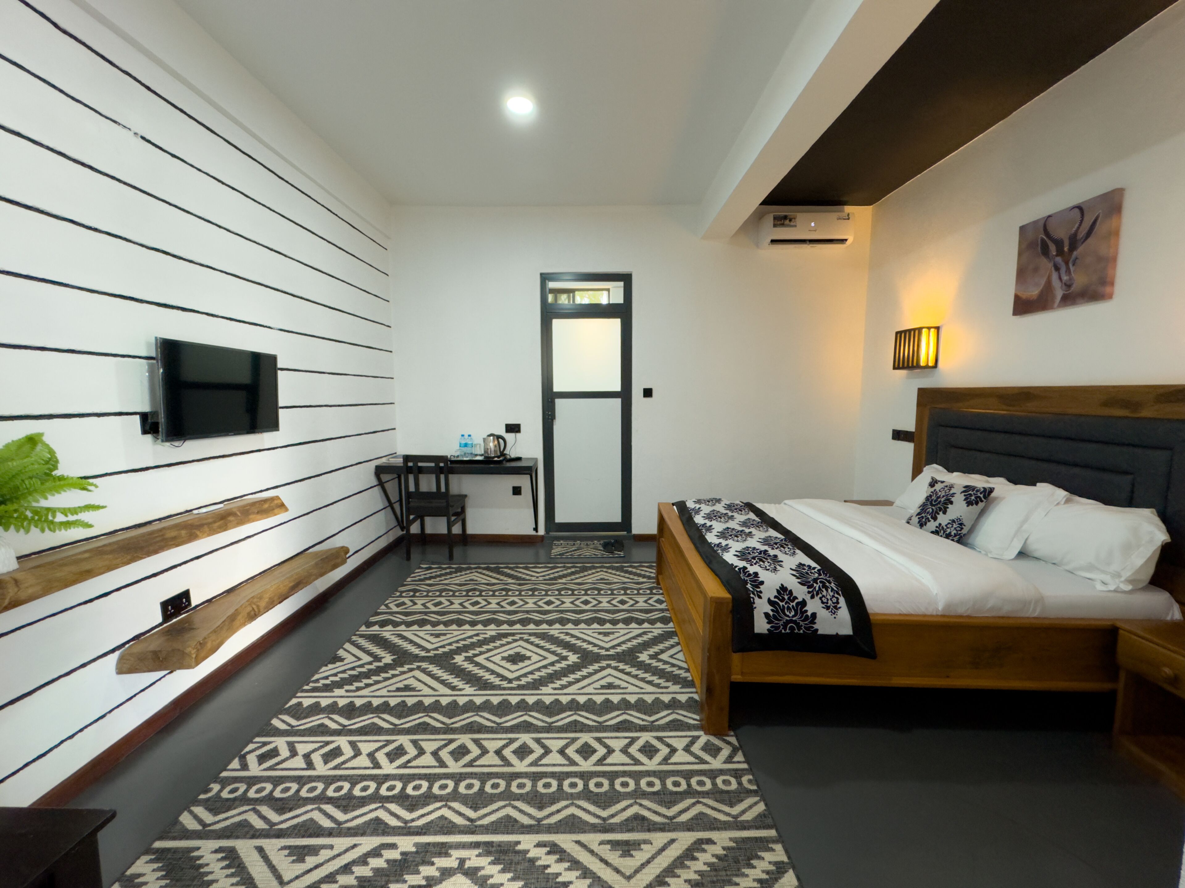 Quarto de hotel moderno com uma cama, uma escrivaninha, uma cadeira, uma televisão e um tapete estampado.