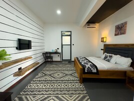 Quarto de hotel moderno com uma cama, uma escrivaninha, uma cadeira, uma televisão e um tapete estampado.