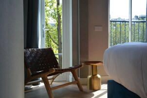 Quarto de hotel moderno com uma cama grande, uma cadeira de madeira e uma pequena mesa.