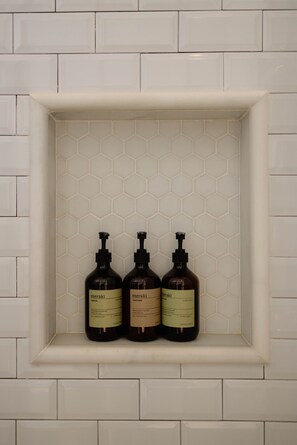 Três frascos de shampoo e condicionador Meraki numa prateleira de azulejos brancos.