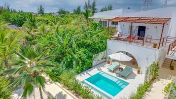 Uma vila branca com piscina, rodeada por vegetação exuberante e palmeiras.