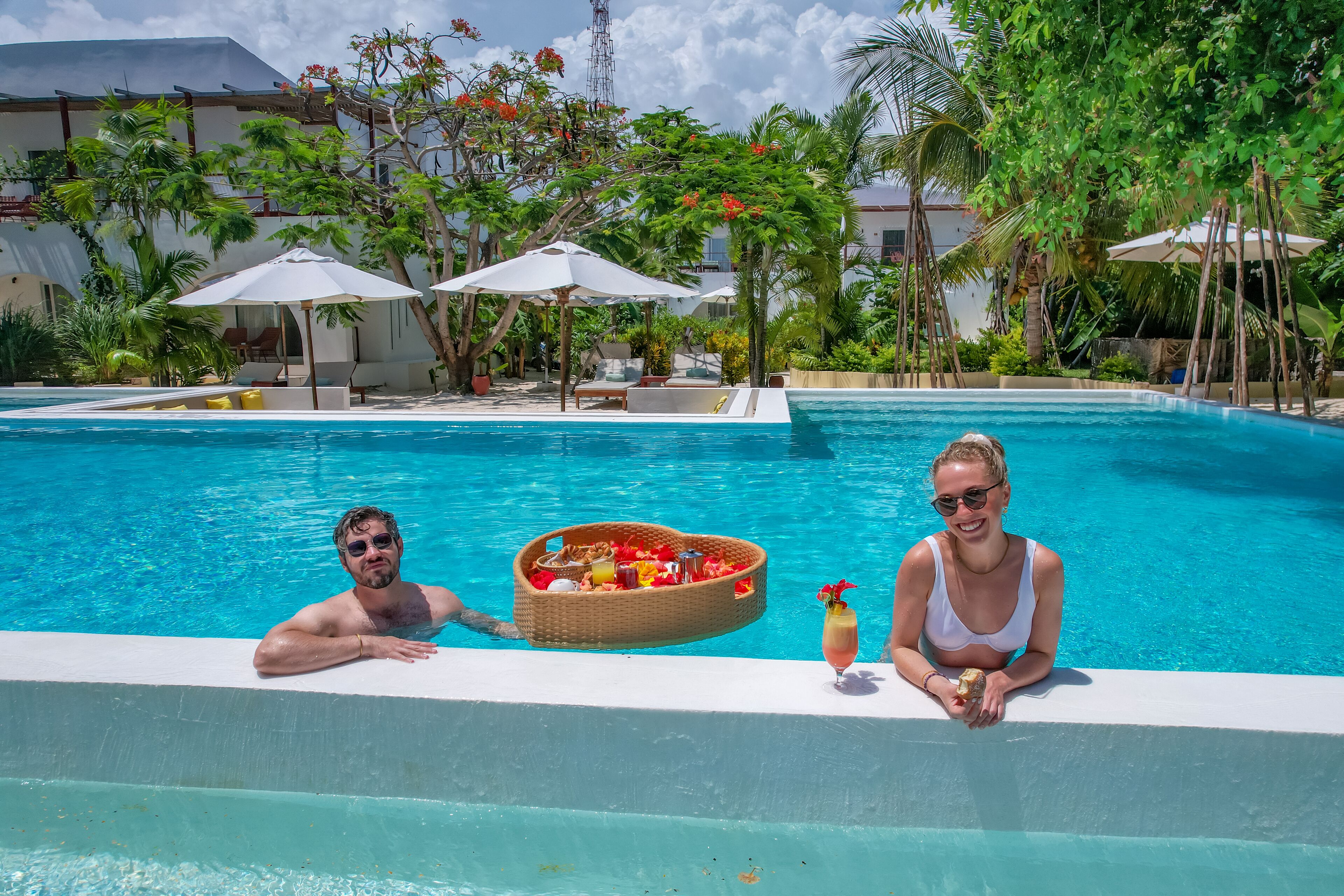 Piscina com espreguiçadeiras e guarda-sóis, cercada por vegetação exuberante.