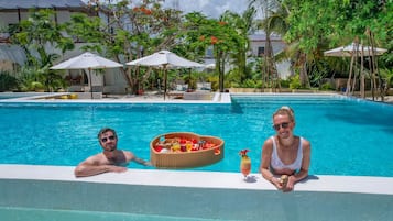 Piscina com espreguiçadeiras e guarda-sóis, cercada por vegetação exuberante.