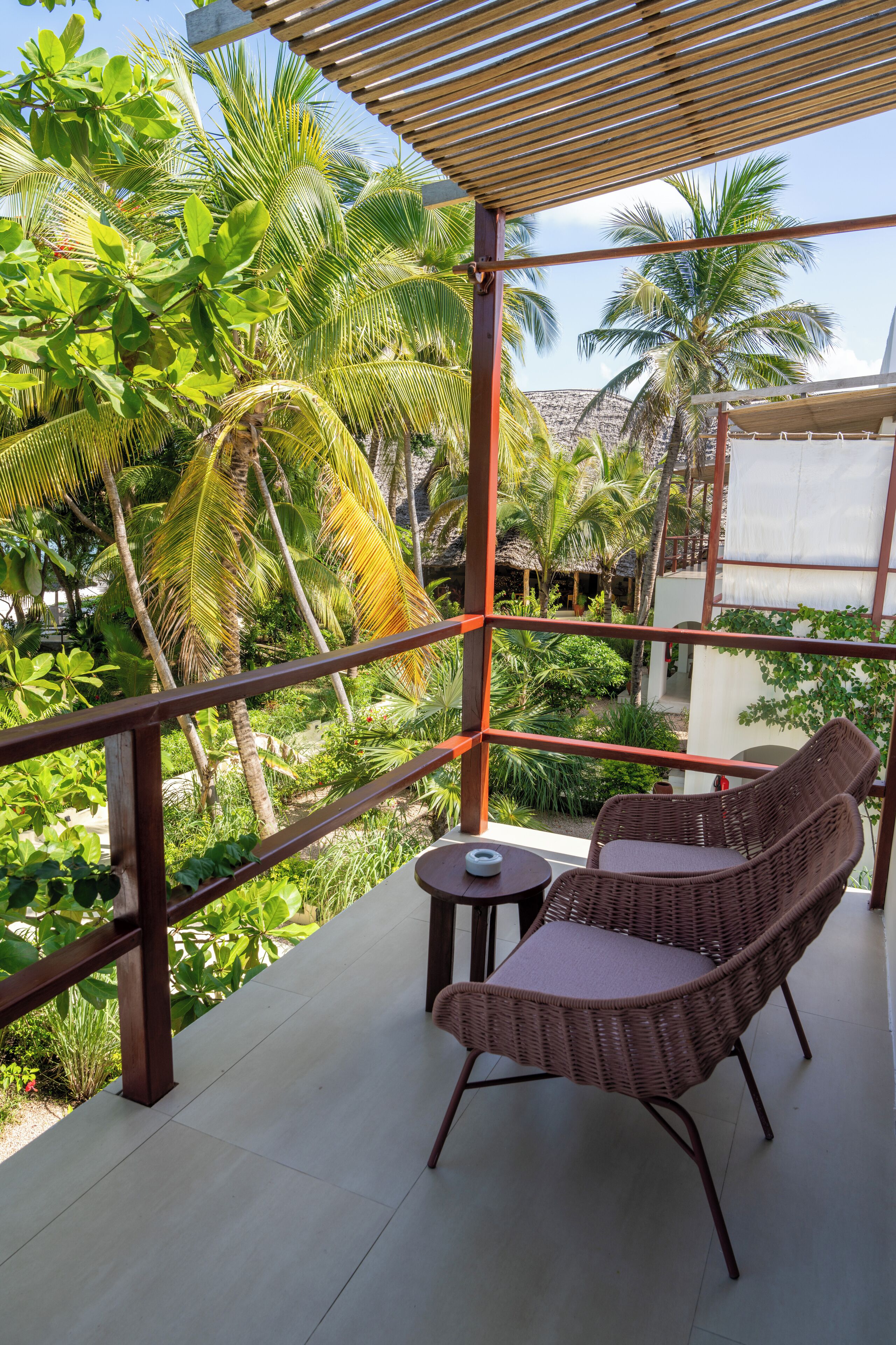 Uma varanda com mobiliário de vime, uma pequena mesa e vista para vegetação tropical e uma montanha ao fundo.