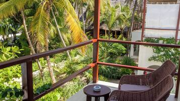 Uma varanda com mobiliário de vime, uma pequena mesa e vista para vegetação tropical e uma montanha ao fundo.