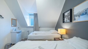 Quarto de hotel moderno com claraboia, uma cama, uma mesa de cabeceira com abajur, espelho, pia e um quadro na parede.