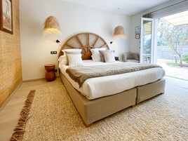 Uma cama grande com cabeceira de madeira, duas luminárias de apoio e vista para o exterior através de uma porta de vidro deslizante.