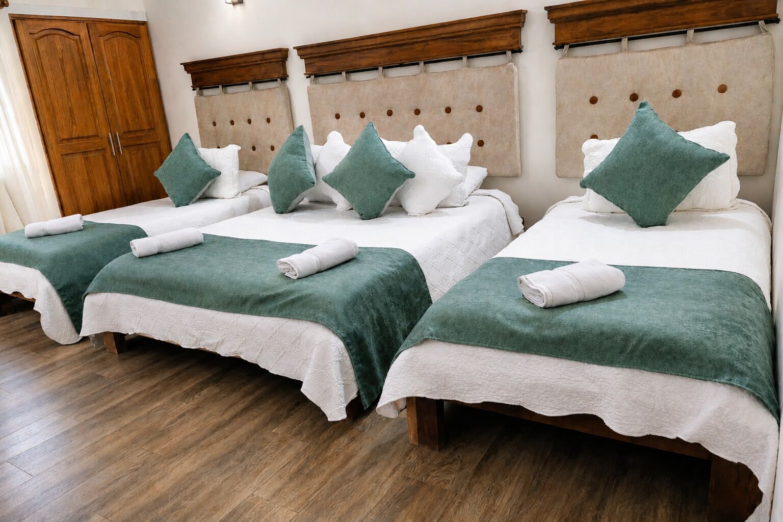 Quarto de hotel com quatro camas, cada uma com colcha verde, almofadas brancas e cabeceira bege.