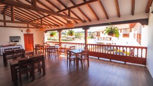 Uma sala de jantar espaçosa com mesas e cadeiras de madeira, teto de madeira e vista para os edifícios e paisagem ao redor.