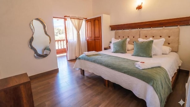 Quarto com cama, piso de madeira, espelho e porta que dá para uma área externa.