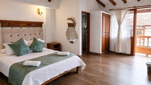 Quarto com uma cama grande, cabeceira de madeira, mesa de cabeceira, espelho e vista para o exterior.