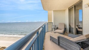 Varanda com vista para o mar, área de estar com mobiliário de vime e porta de vidro que dá para o interior.