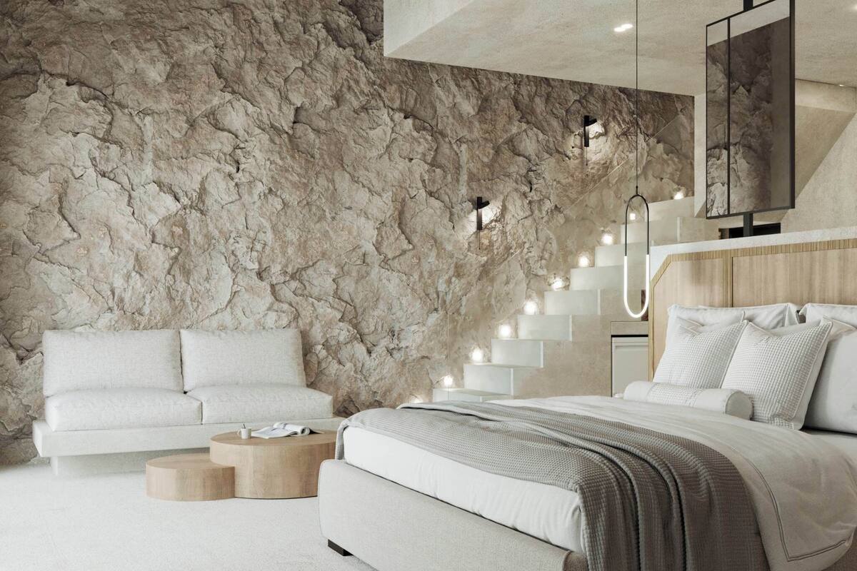 Um quarto com uma cama grande, um sofá branco, uma mesa de centro de madeira e uma parede de pedra.