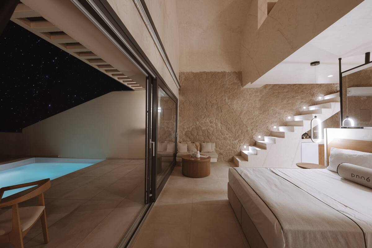 Quarto moderno com cama grande, área de estar com uma mesa e escada para um andar superior.