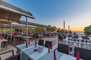 Um restaurante ao ar livre com mesas e cadeiras, área coberta e vista para o mar.