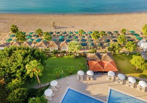 Vista aérea de um resort com piscina, praia e área de lounge com guarda-sóis.