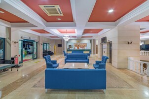 Um hall amplo com sofás azuis, um balcão de recepção e um lustre.