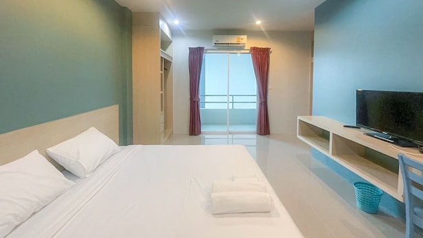 Quarto de hotel com uma cama grande, televisão sobre um suporte, uma escrivaninha e janela com cortinas.