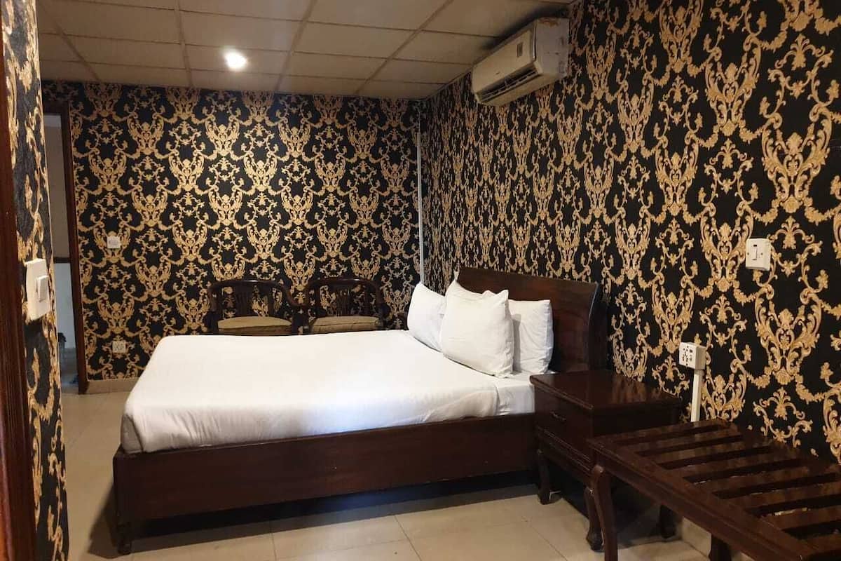 Quarto com uma cama grande, uma mesa de cabeceira, um banco de madeira e um ar condicionado fixado na parede.