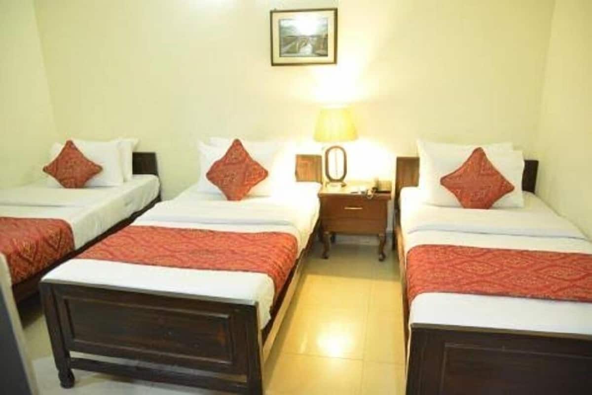 Quarto de hotel com duas camas de solteiro, cada uma com colcha vermelha e almofadas combinando. Há uma mesinha de cabeceira com abajur entre as camas.