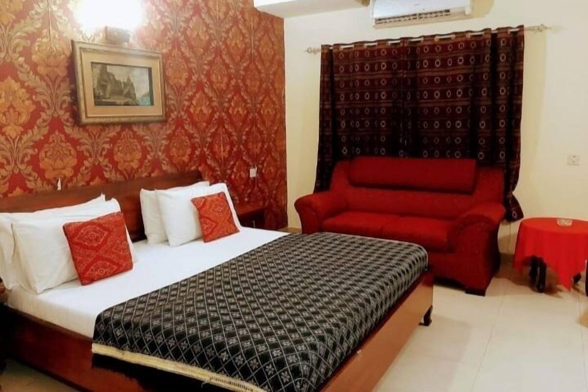 Quarto de hotel com uma cama, um sofá vermelho e uma cortina estampada.