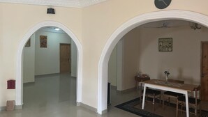 Um corredor espaçoso com área de jantar, mesa e cadeiras, um relógio na parede e uma porta no final.