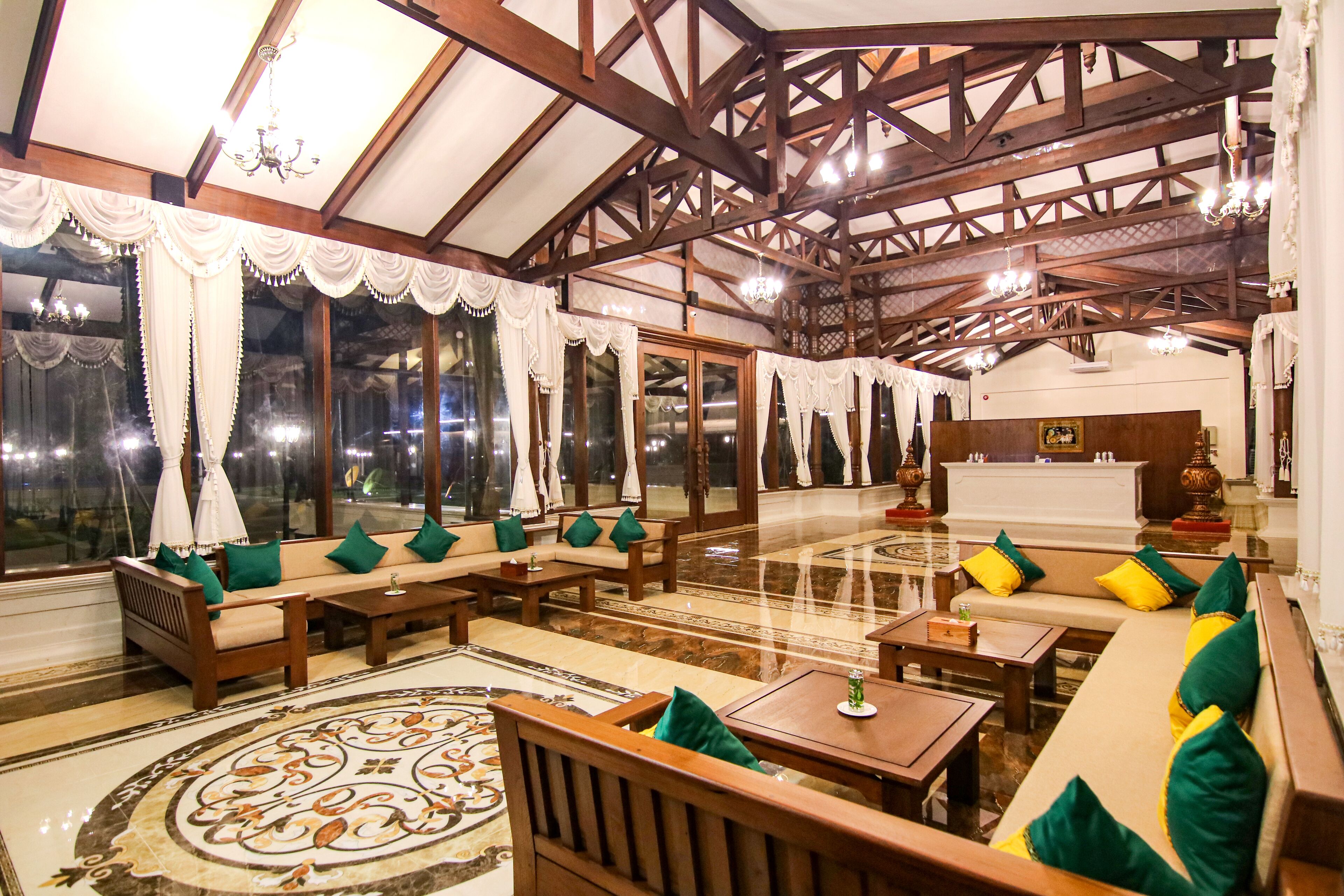 Um hall amplo com móveis de madeira, grandes janelas com cortinas e um lustre.