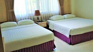 Quarto de hotel com duas camas, uma mesa de cabeceira com abajur e cortinas finas.