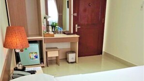 Quarto de hotel com cama, escrivaninha, luminária, espelho e porta.