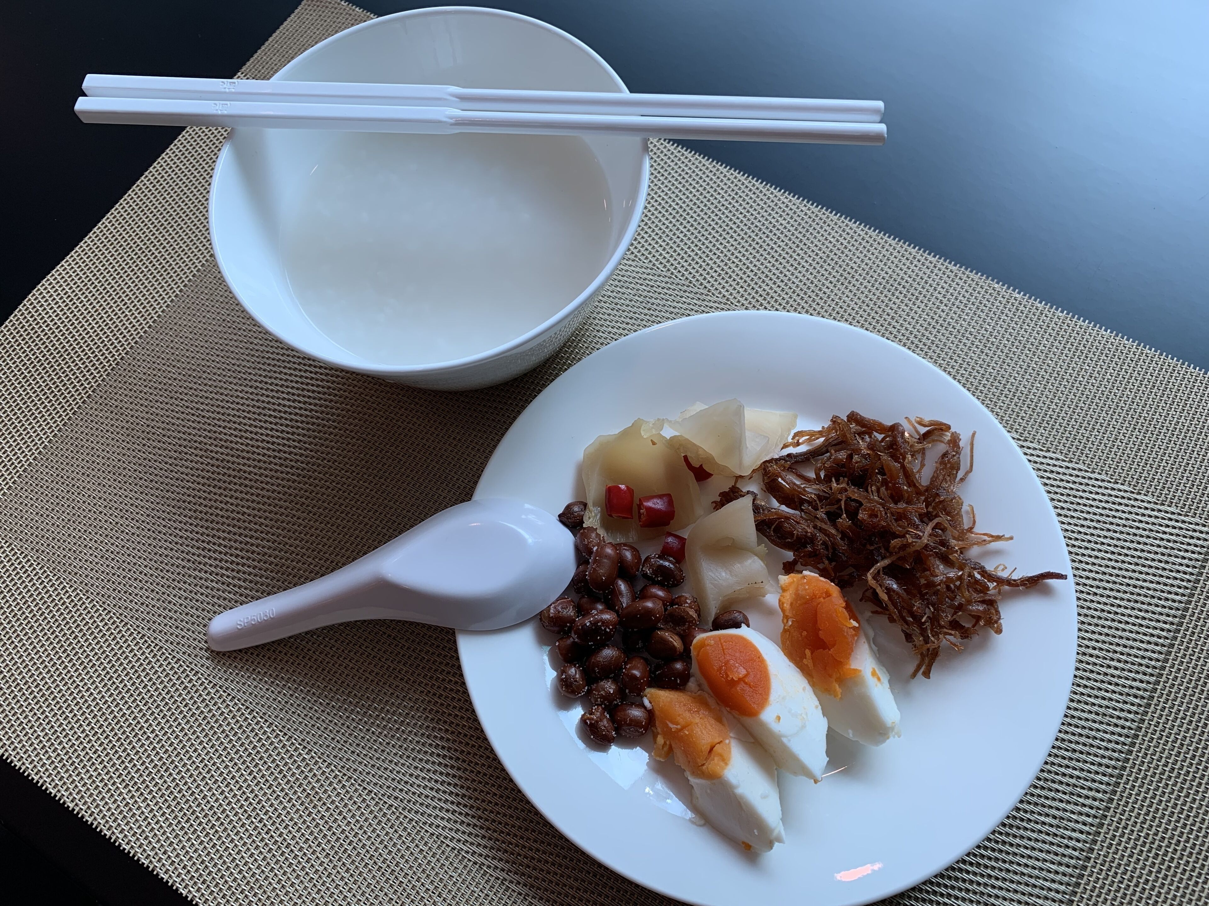 Prato com tofu, feijão e carne desfiada, uma tigela branca e pauzinhos sobre uma mesa com jogo americano tecido.