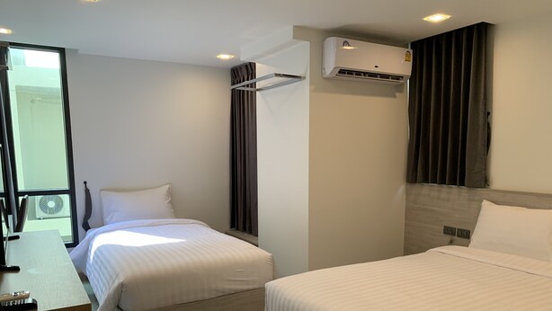 Quarto de hotel moderno com duas camas, uma escrivaninha e uma janela grande.