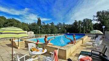 Área de piscina com espreguiçadeiras, guarda-sóis e uma mesa com frutas e bebidas.