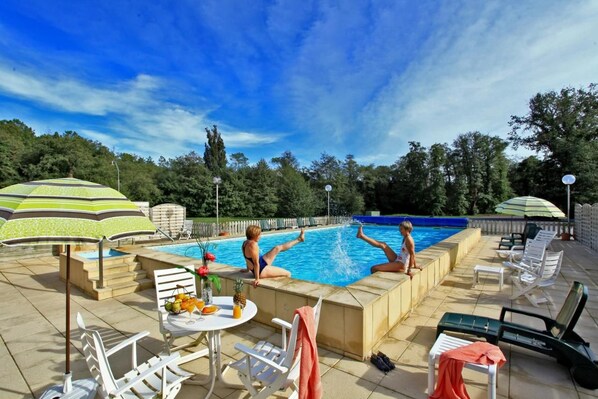 Área de piscina com espreguiçadeiras, guarda-sóis e uma mesa com frutas e bebidas.