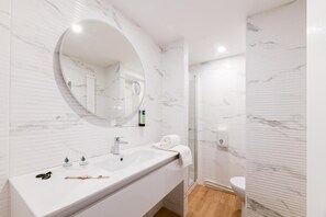 Casa de banho com toucador de mármore, espelho redondo, toalha e cabine de duche com vidro.