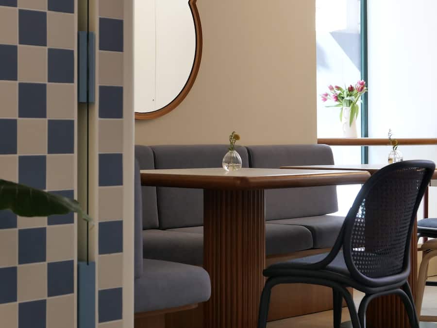 Um interior moderno com parede quadriculada, um espelho redondo, uma mesa de madeira, um sofá cinza e uma cadeira preta.