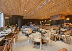 Um restaurante moderno com teto de madeira, mesas redondas e assentos acolchoados.