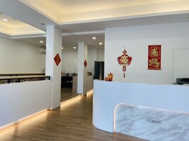 Um lobby de hotel moderno com uma mesa de recepção, piso de madeira e decorações vermelhas tradicionais nas paredes.
