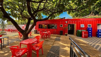 Um edifício vermelho com área externa para sentar, uma árvore e um refrigerador de Coca-Cola.