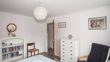 Quarto com cama, estante, penteadeira, cadeira e porta que dá para outro cômodo.