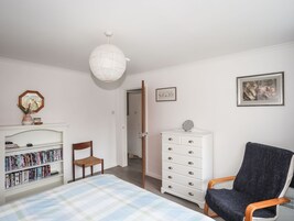 Quarto com cama, estante, penteadeira, cadeira e porta que dá para outro cômodo.