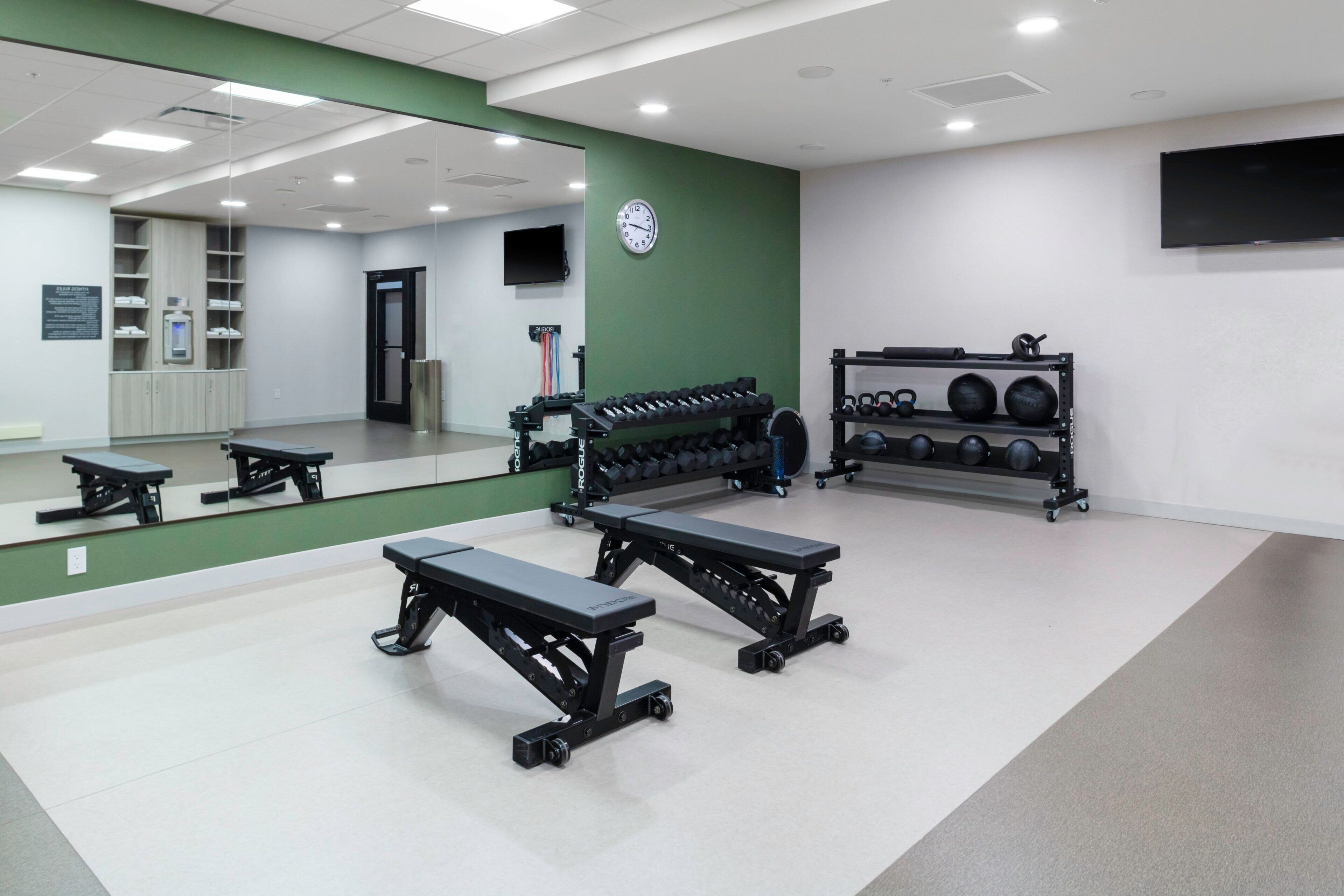Uma academia com equipamentos de musculação, bancos e um espelho grande na parede.