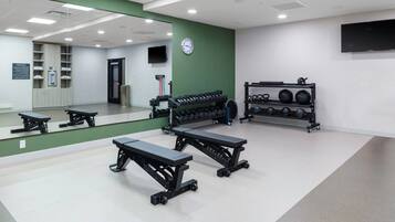 Uma academia com equipamentos de musculação, bancos e um espelho grande na parede.