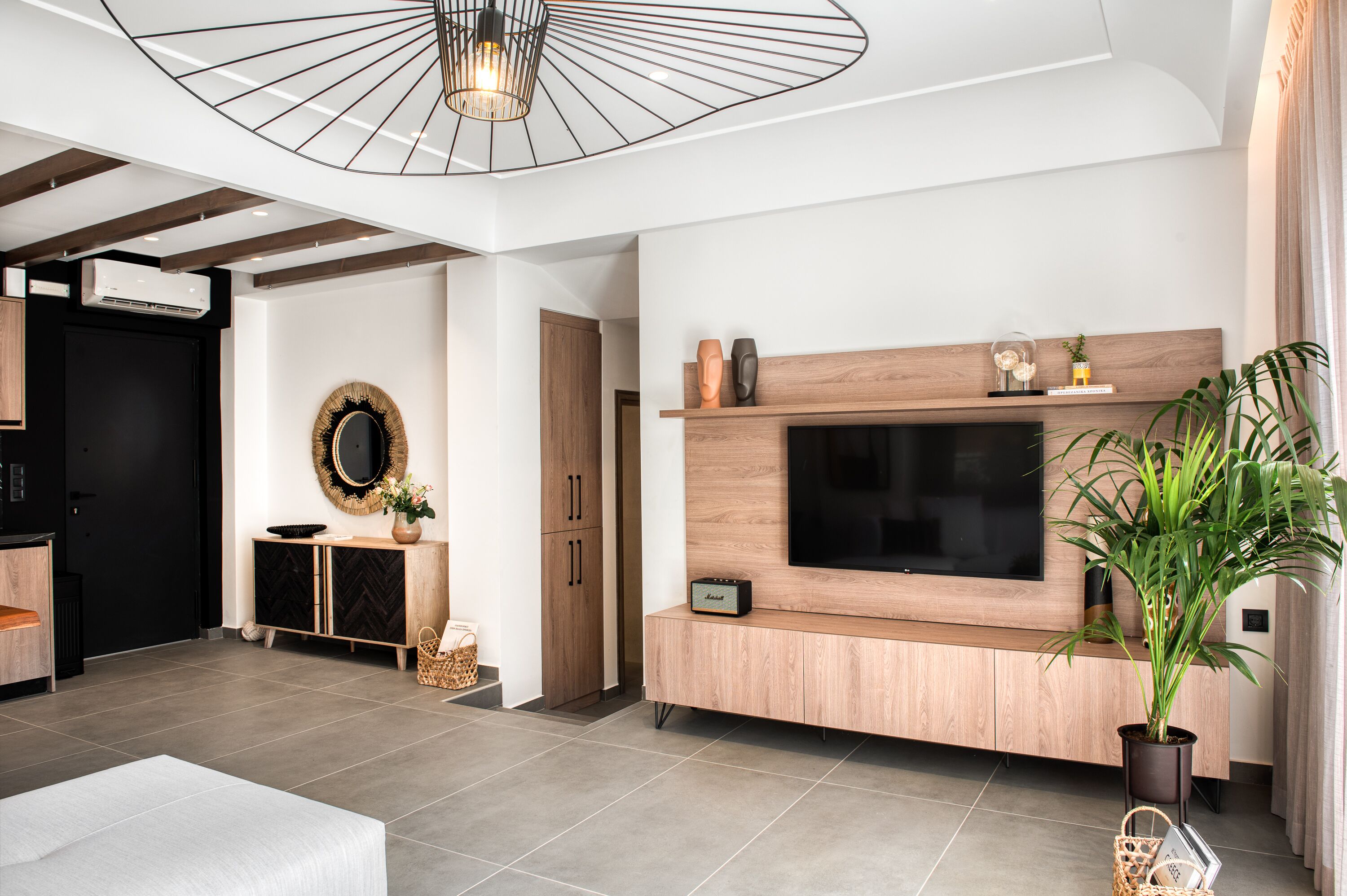 Uma sala de estar moderna com uma grande TV de tela plana fixada em uma parede de madeira, um ventilador de teto e um vaso com planta.