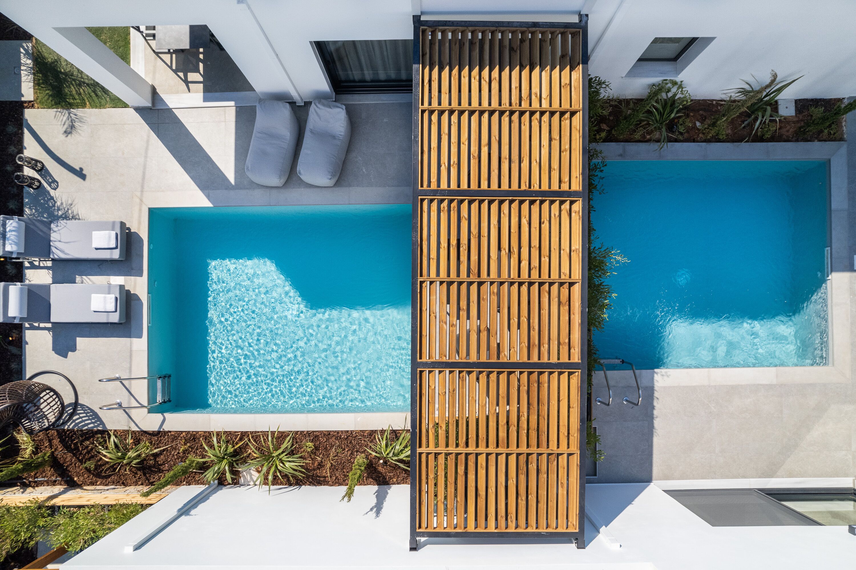 Piscina no terraço com cerca de madeira, cadeiras de descanso e um pequeno jardim.