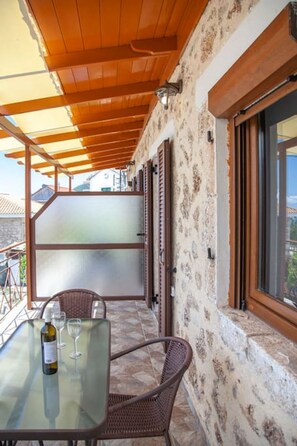 Uma área de estar coberta ao ar livre, com uma mesa, cadeiras, uma garrafa de vinho e vista para os edifícios ao redor.