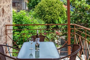 Uma mesa com duas taças de vinho e uma garrafa, colocada numa varanda com grades de metal e vegetação ao fundo.