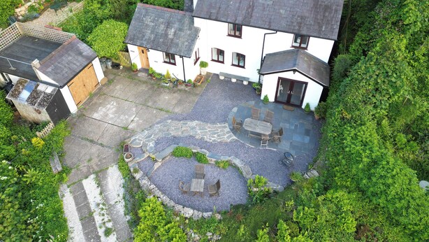 Uma casa de dois andares com um alpendre de pedra e área de estar ao ar livre.