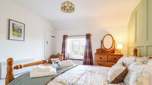 Um quarto com cama, cômoda, espelho, janela com cortinas e luminária suspensa.