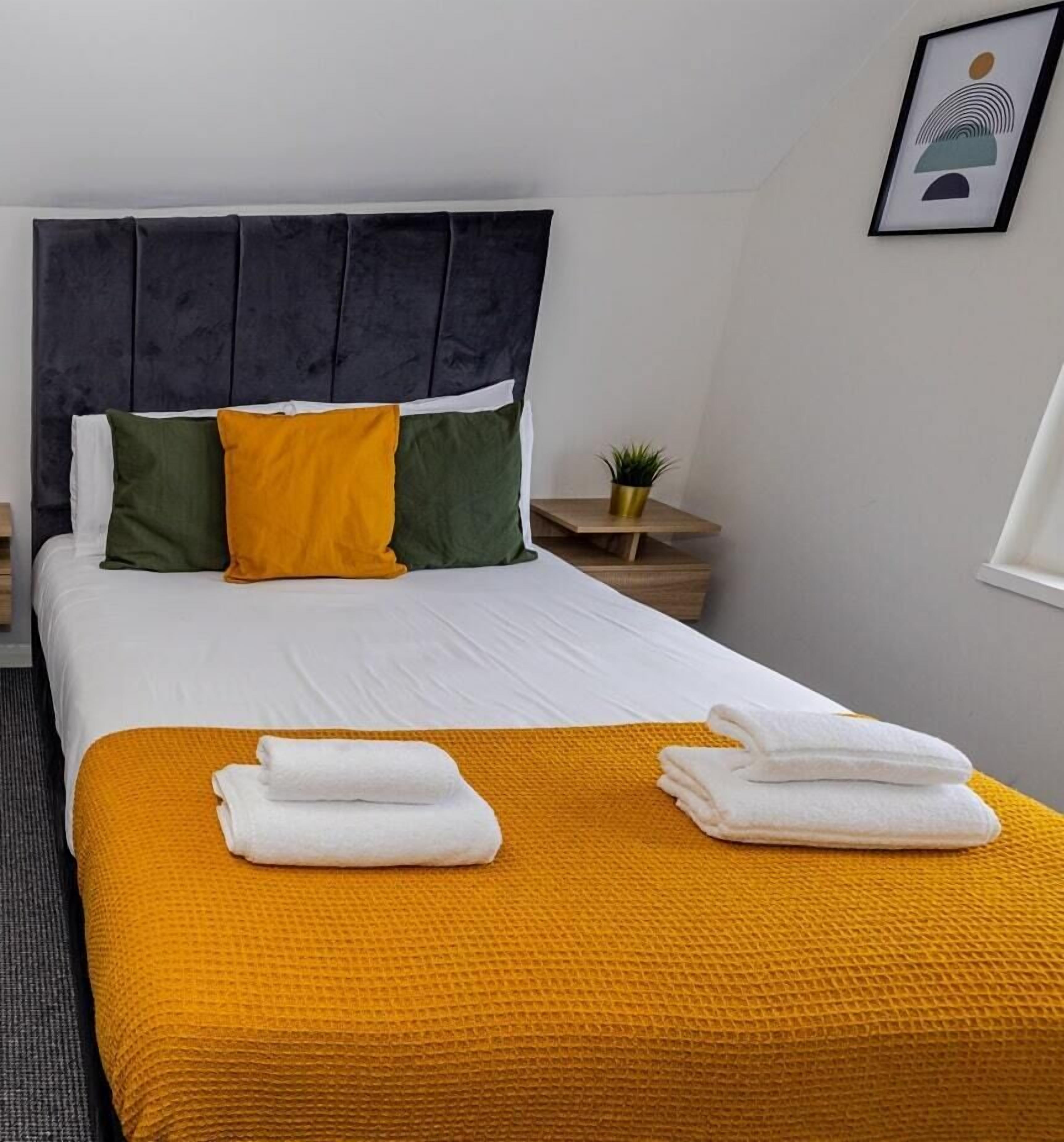 Quarto de hotel com cama, mesa de cabeceira, planta em vaso e quadro pendurado na parede.