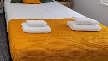 Quarto de hotel com cama, mesa de cabeceira, planta em vaso e quadro pendurado na parede.